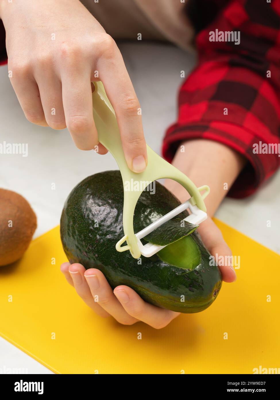 A child holds an avocado in one hand and peels the skin with a ...
