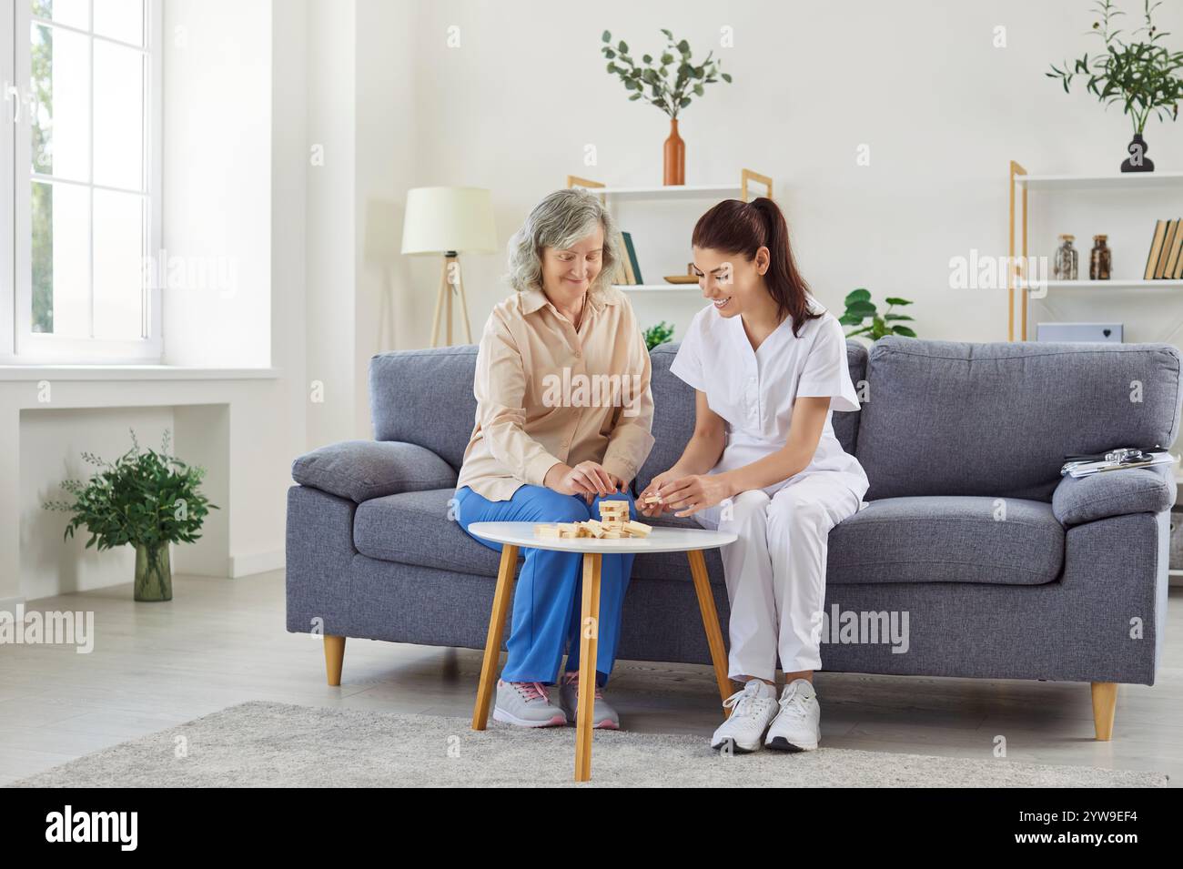 Young nurse playing with senior elderly person with wooden building ...
