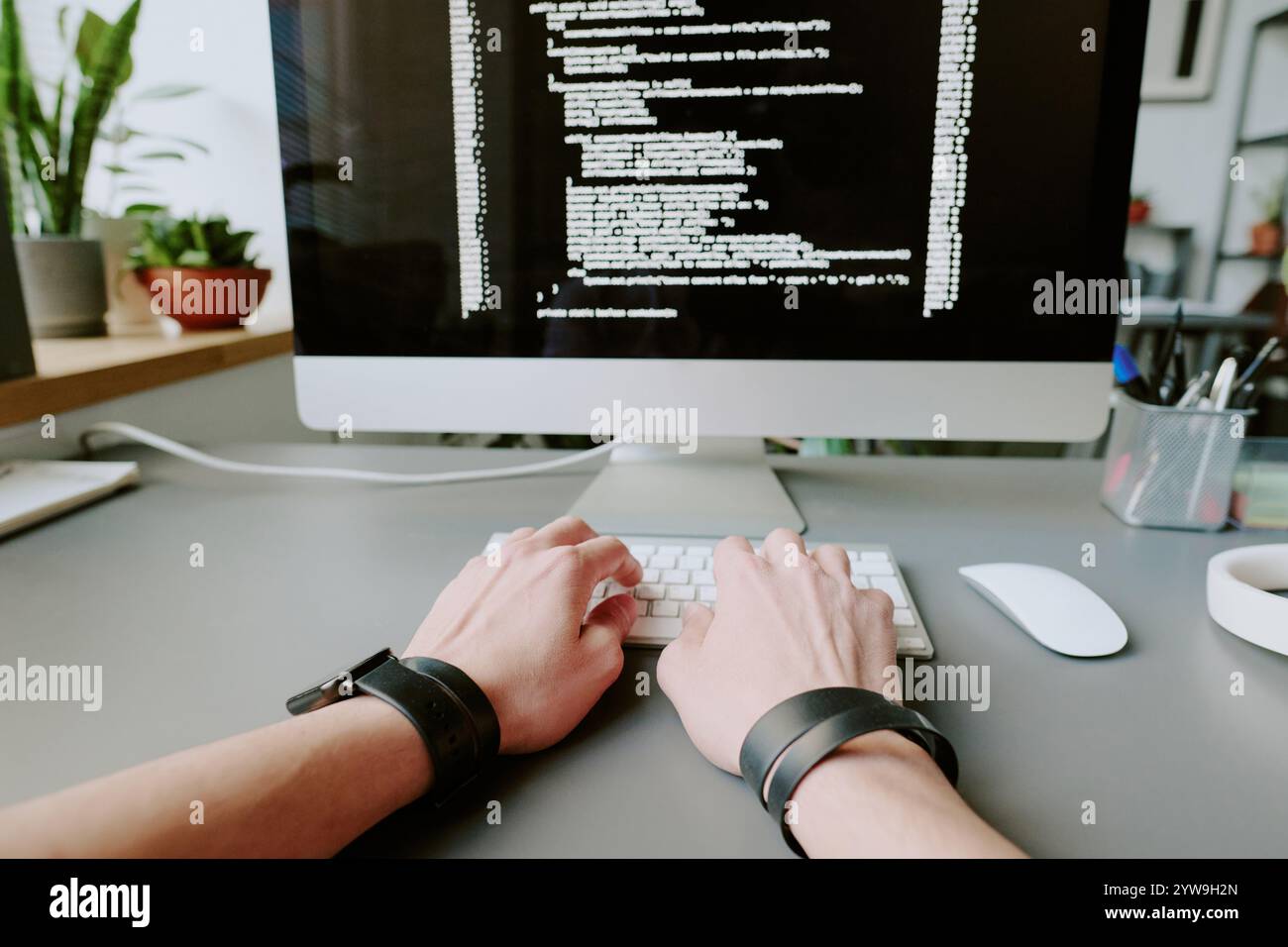 Medium close up of unrecognizable male hands typing codes on white keyboard, computer monitor ...