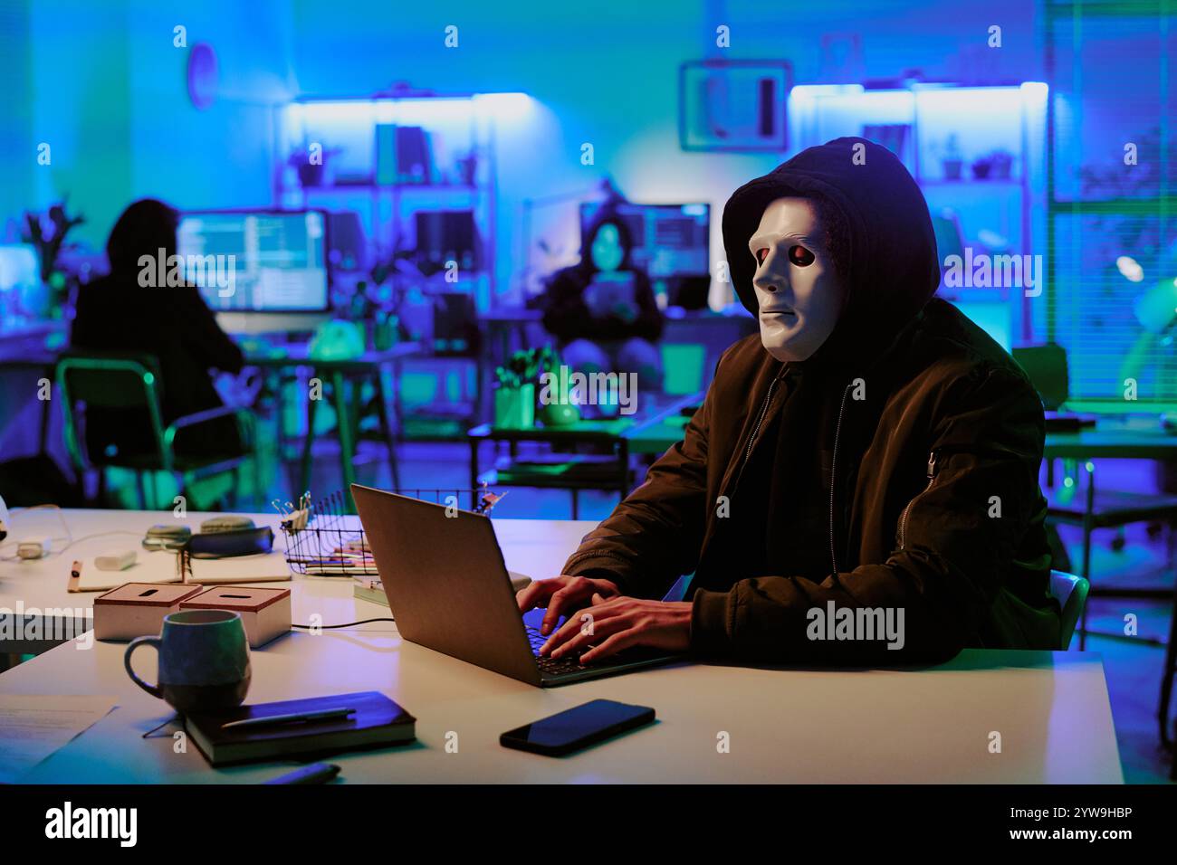 Medium close up of hacker wearing black hoodie and white mask hiding ...
