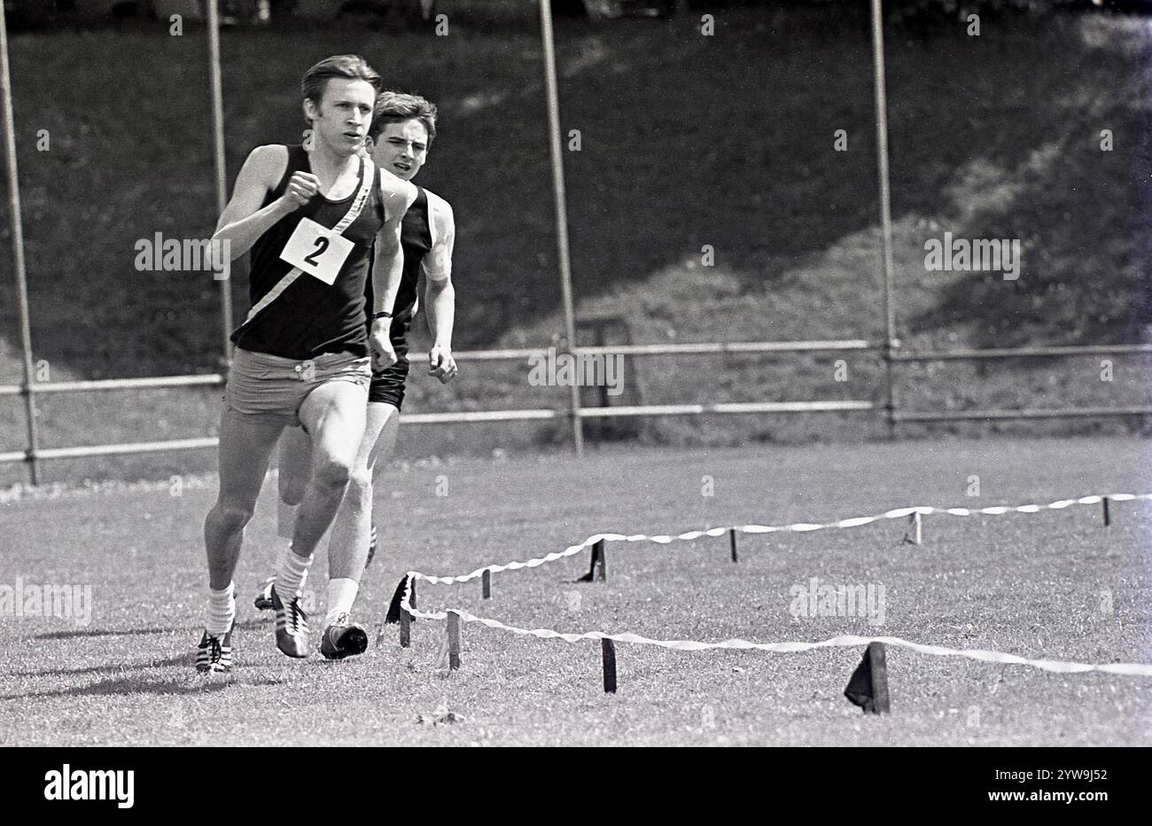 1968, historiclal, two young men competing in a running race outside on a grass track, England ...