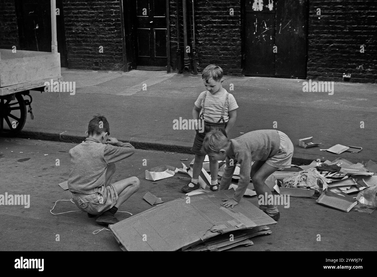 Three young boys playing with cardboard boxes in street after close of ...