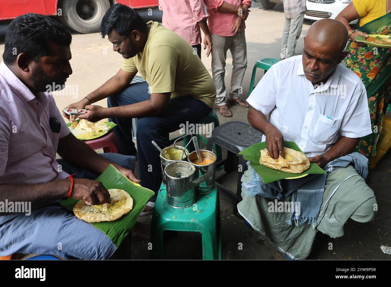 Men eating puri using a banana leaf as a plate at a street food stall ...