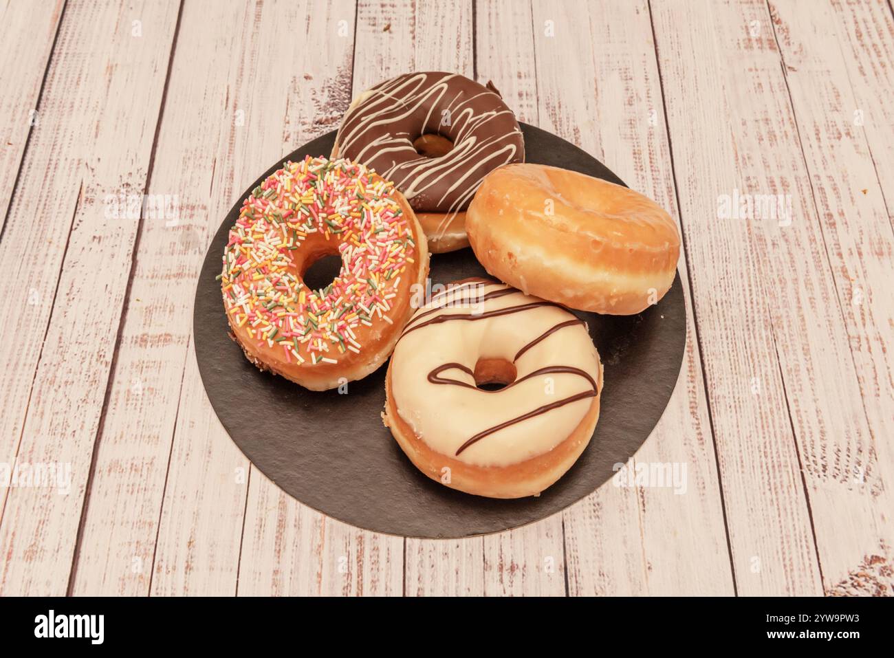 Four donuts of different flavors on a black circular tray Stock Photo ...
