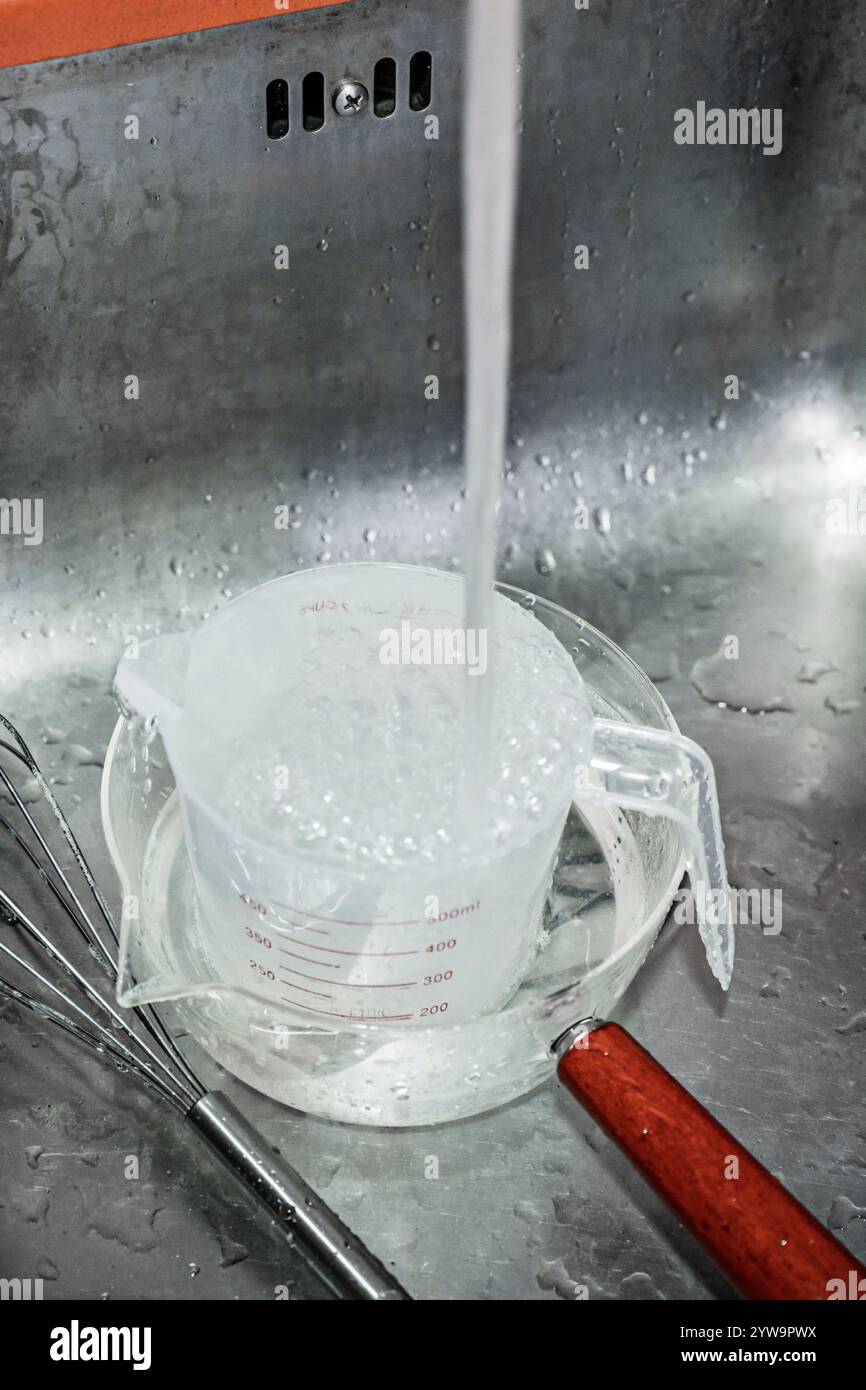 Wash kitchen utensils under running tap water in a stainless steel sink ...