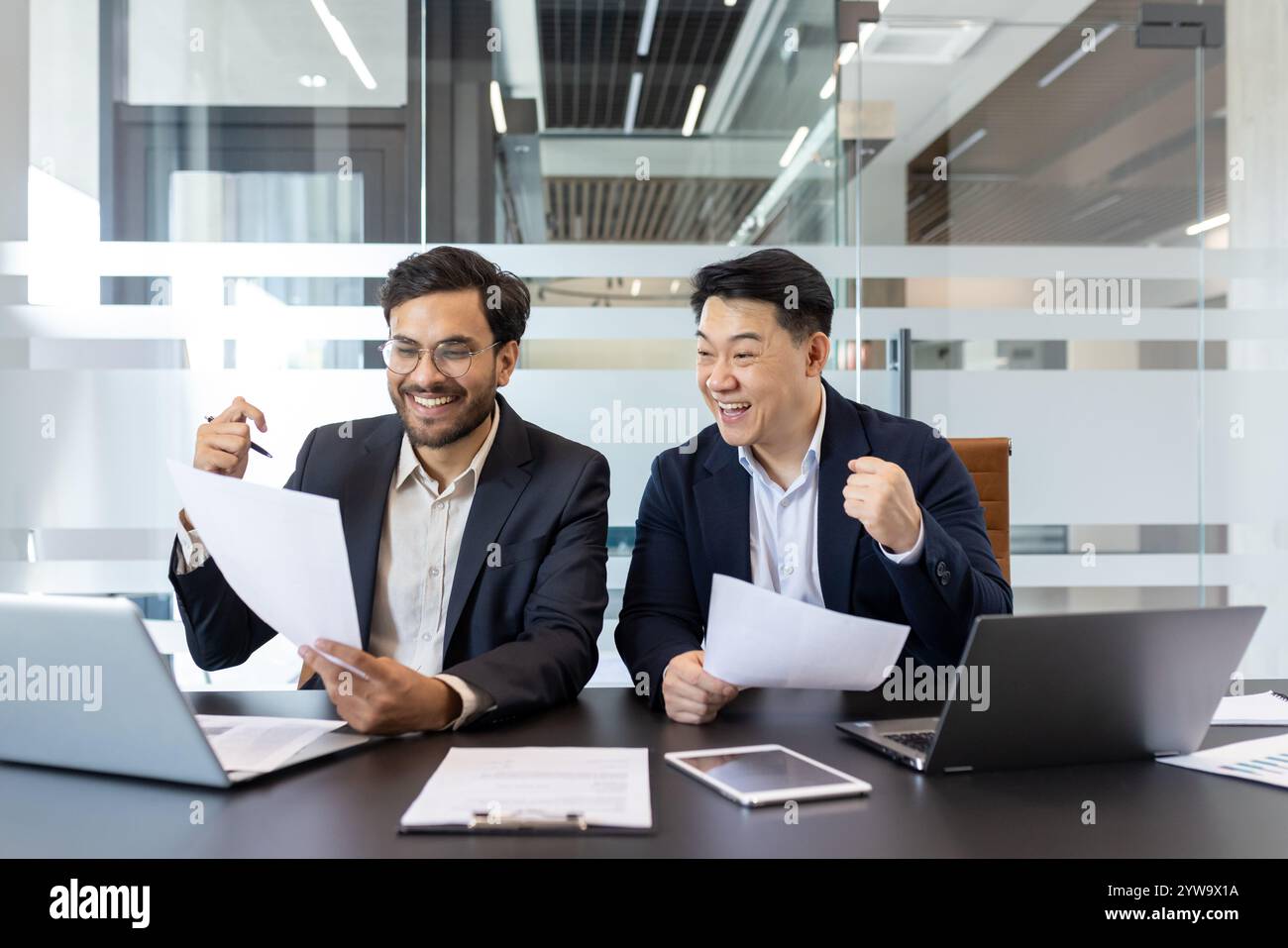 Two excited businessmen review successful documents while working on ...