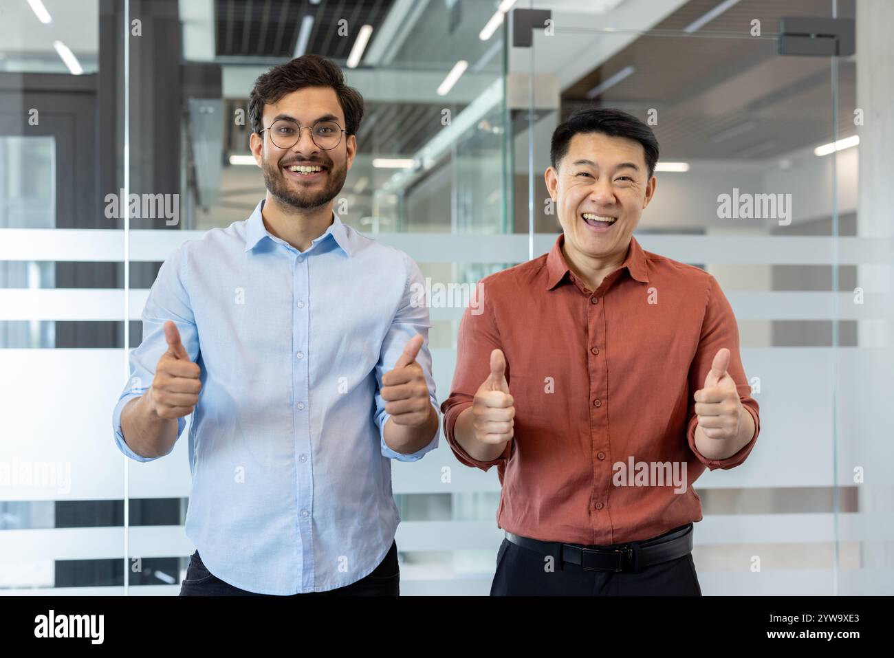 Two smiling men in an office setting, expressing positivity with thumbs ...