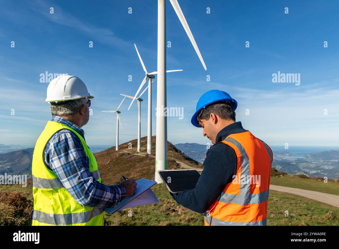 Two engineers wearing safety vests and helmets are inspecting wind ...