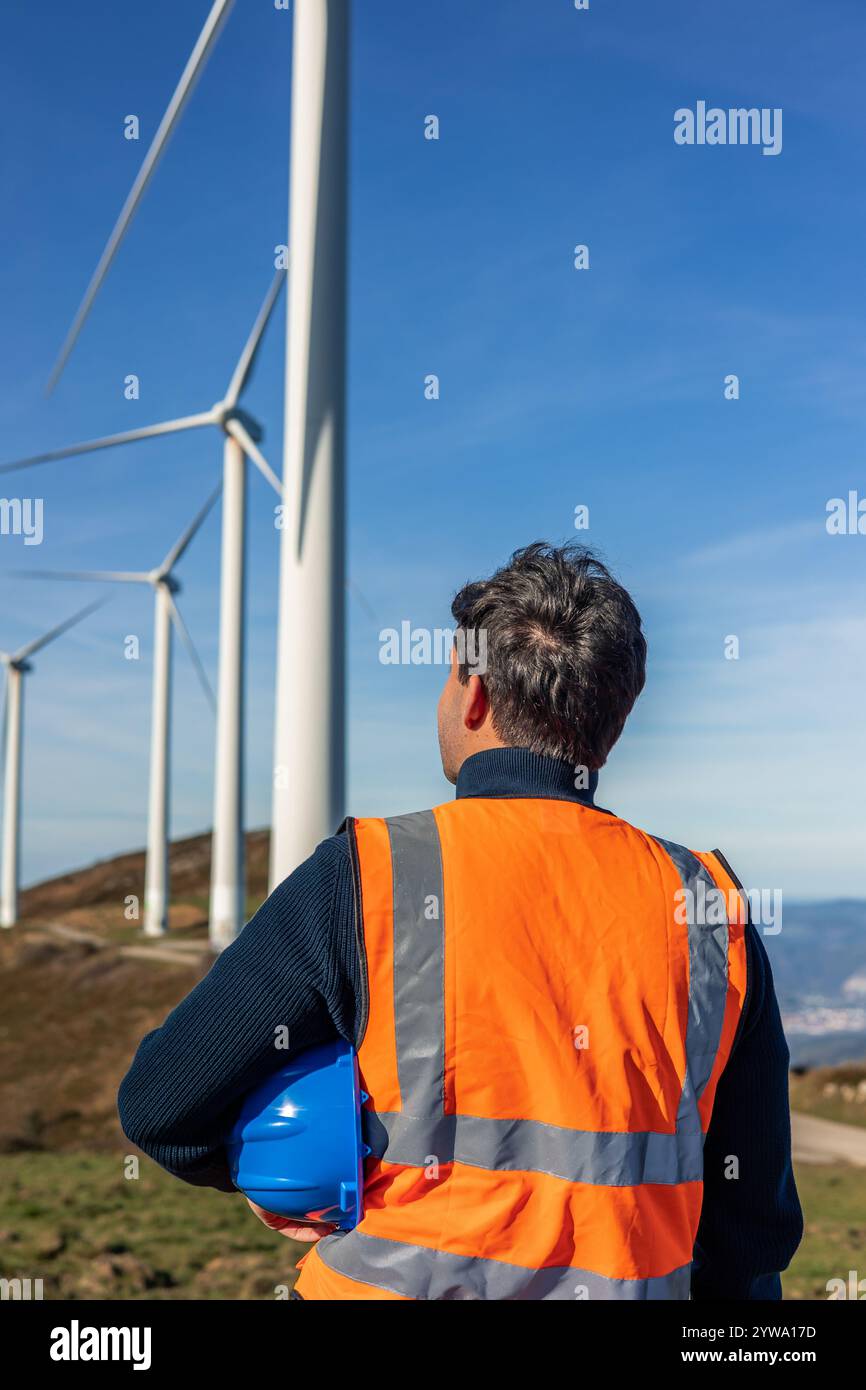 Engineer wearing an orange safety vest holds a blue helmet while ...