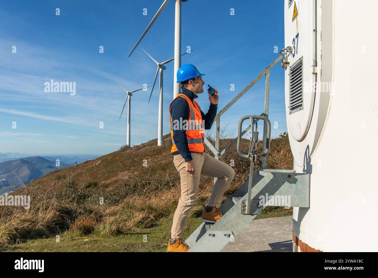 latin Engineer wearing an orange safety vest and blue hardhat climbing ...