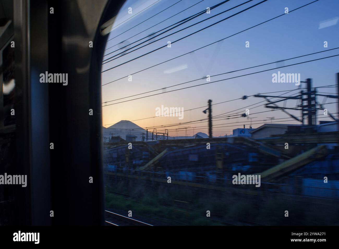 Mount Fuji silhouetted against sunset sky, view from Japanese shinkansen bullet train in Tokyo ...