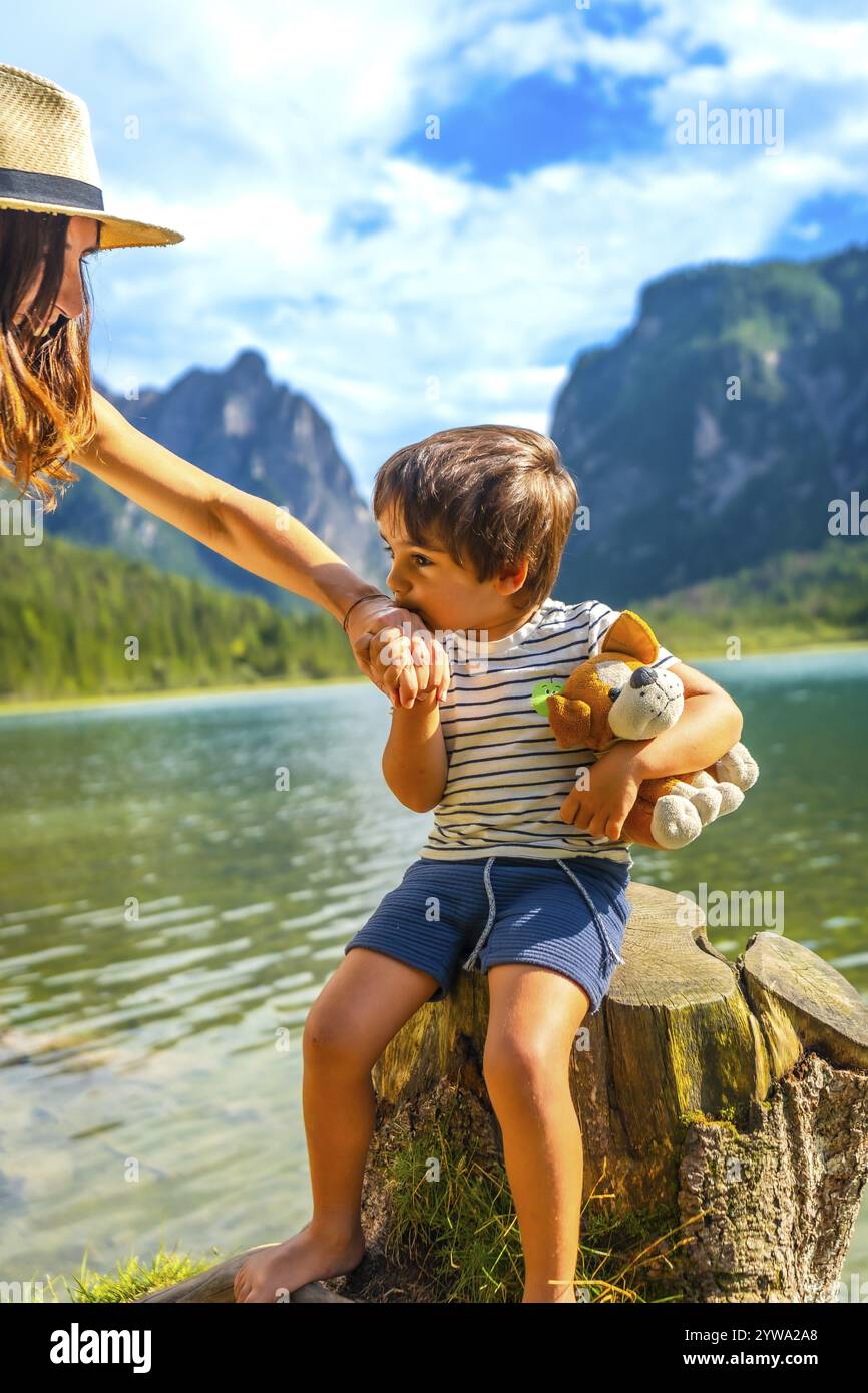 Mother gently holding hands with her son, sitting on a tree stump by a ...