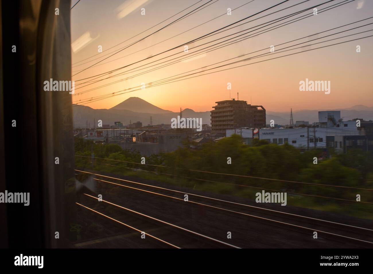 Mount Fuji silhouetted against sunset sky, view from Japanese shinkansen bullet train in Tokyo ...
