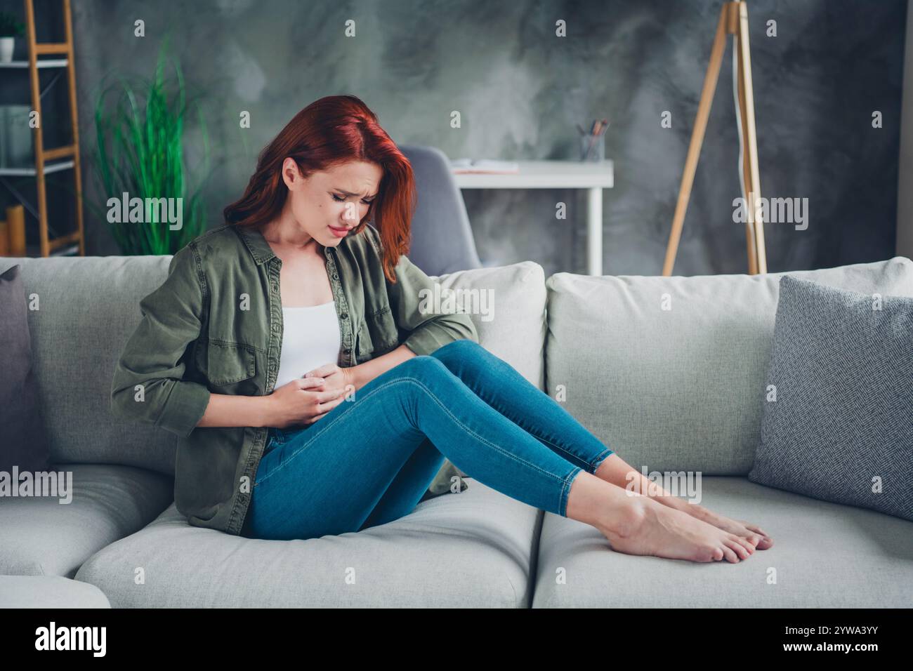 Full body photo of nice young ginger girl sit sofa stomach ache suffer ...