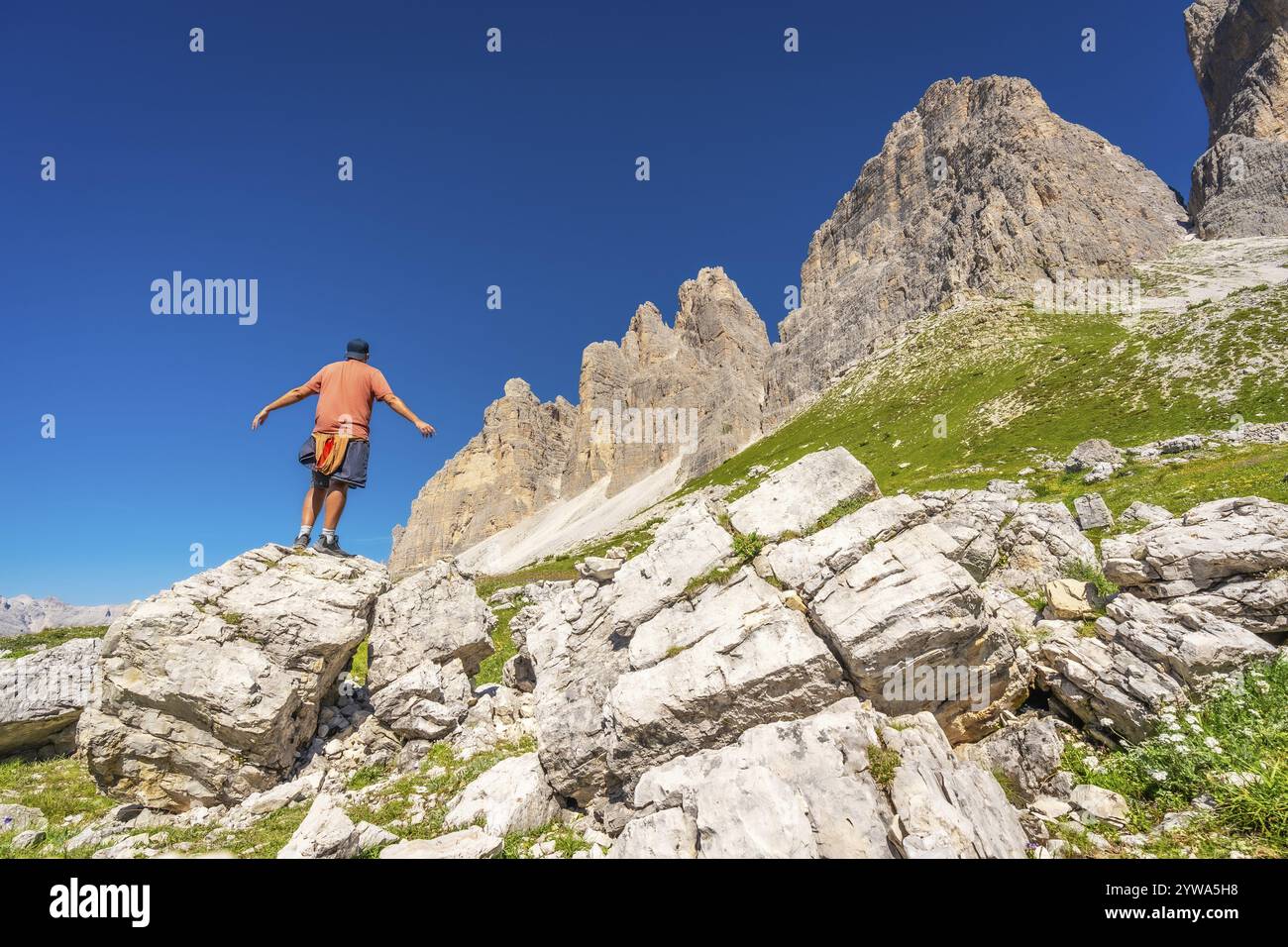 Tourist balancing on a rock formation with tre cime di lavaredo in the ...