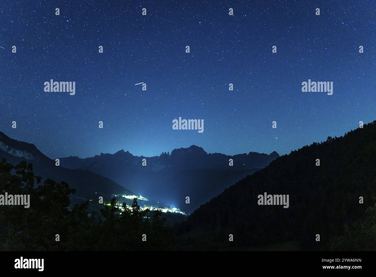 Airplane flying over a mountain valley with an illuminated village at ...