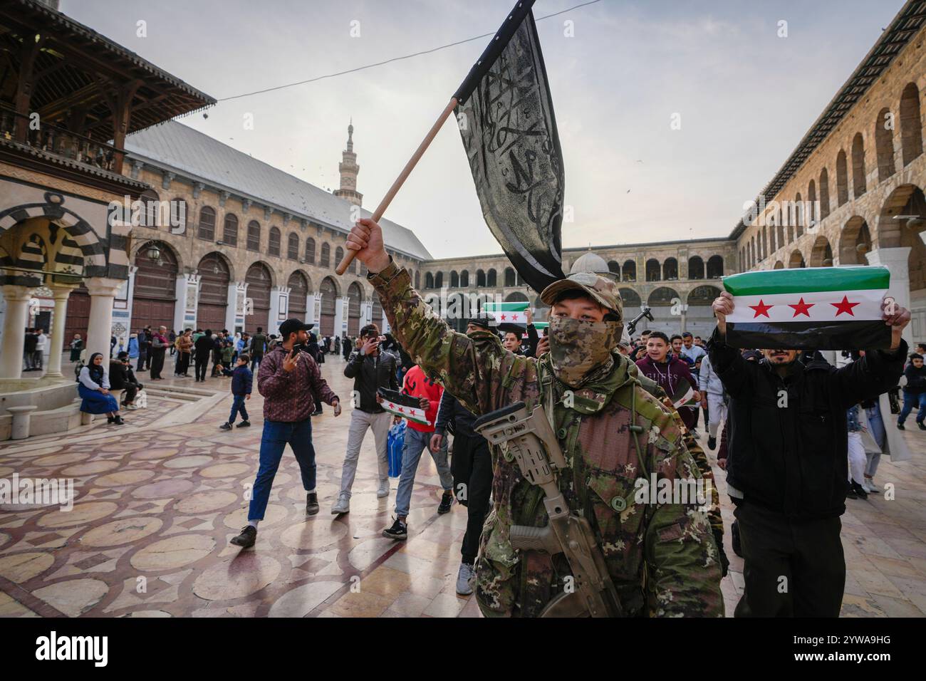 A masked opposition fighter carries a flag of Hayat Tahrir al-Sham (HTS) in the courtyard of the ...