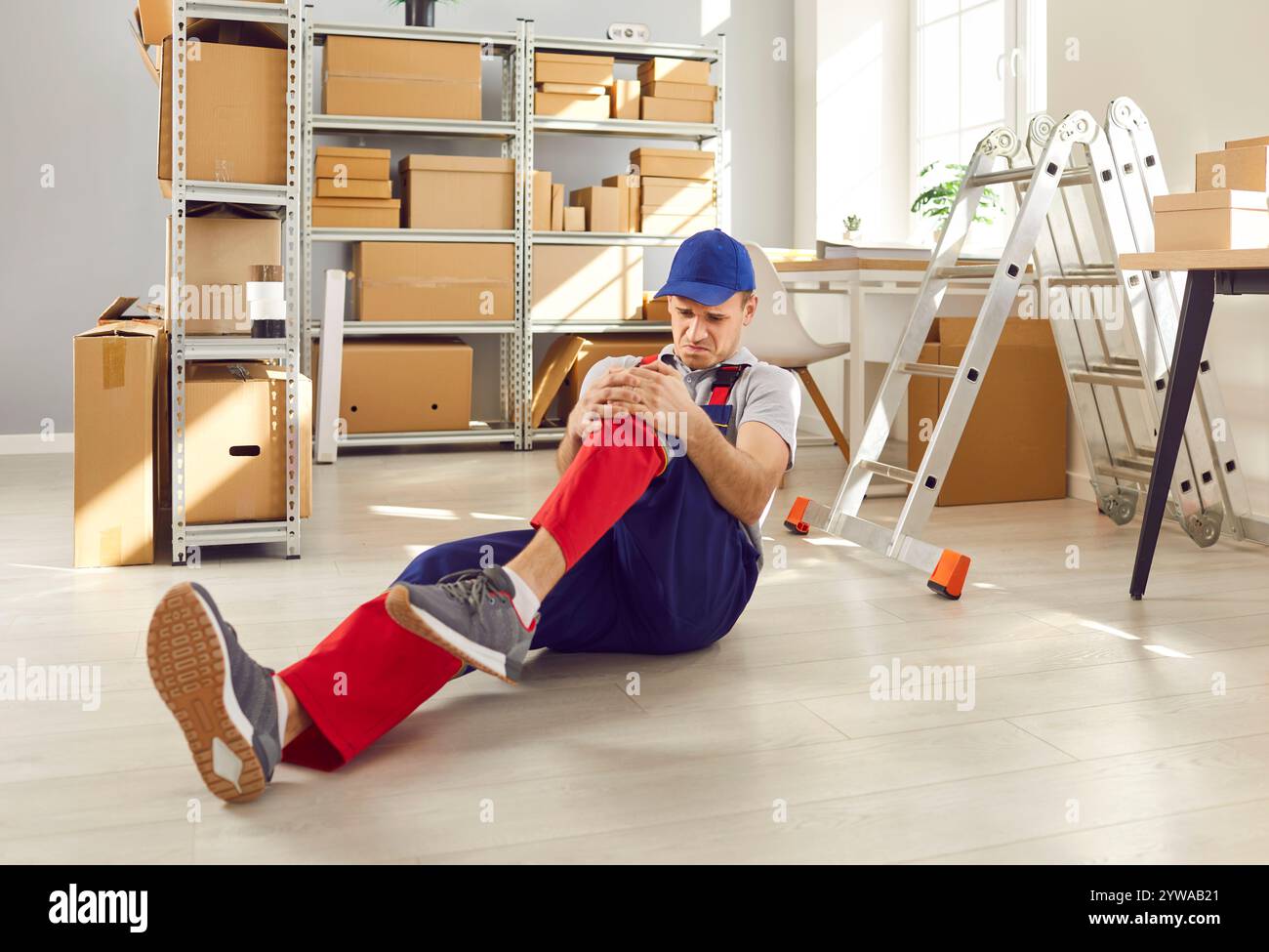 Male worker storekeeper in overall sitting on the floor in warehouse ...