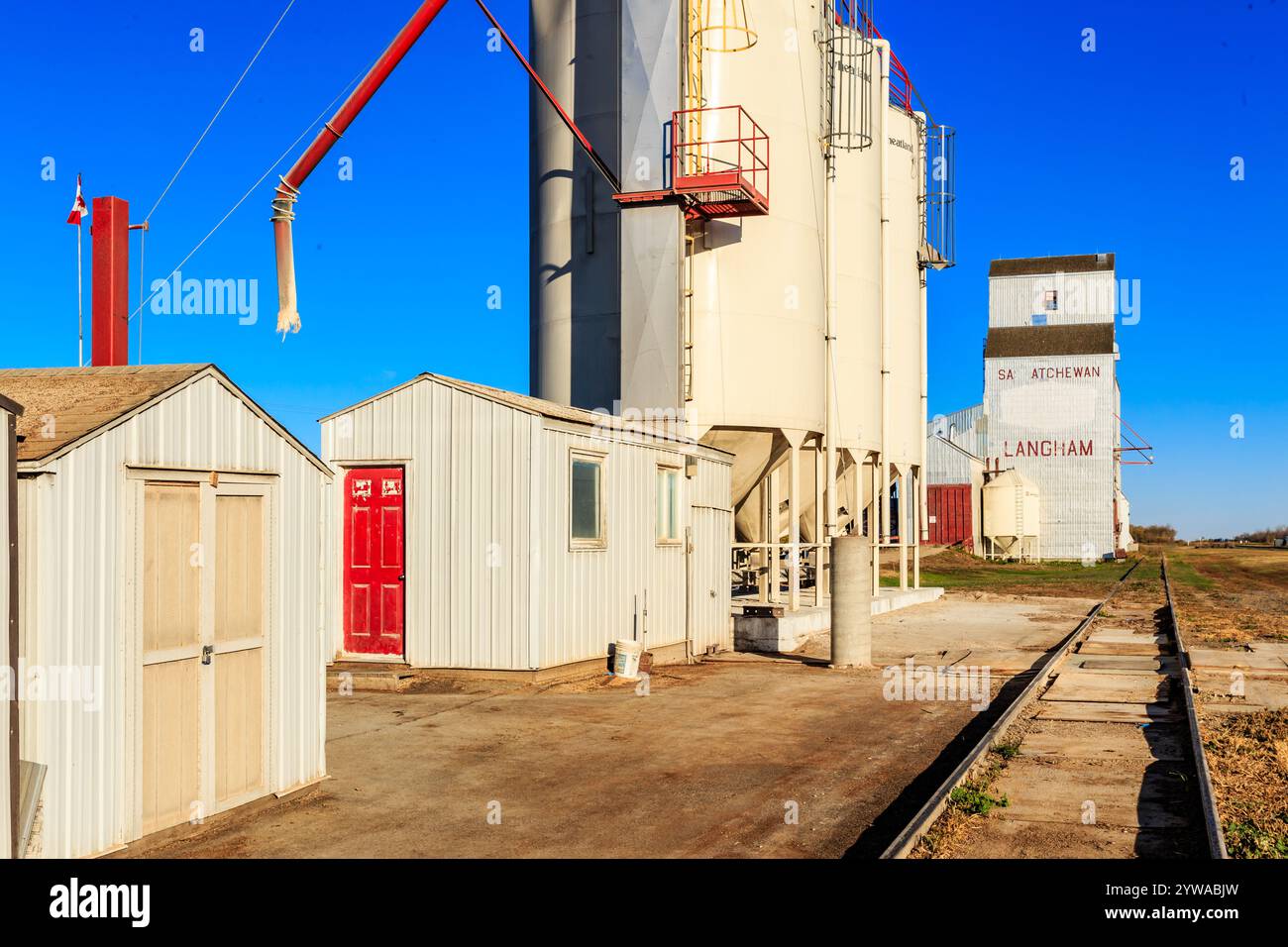 A large grain silo is next to a small building. The silo is white and ...