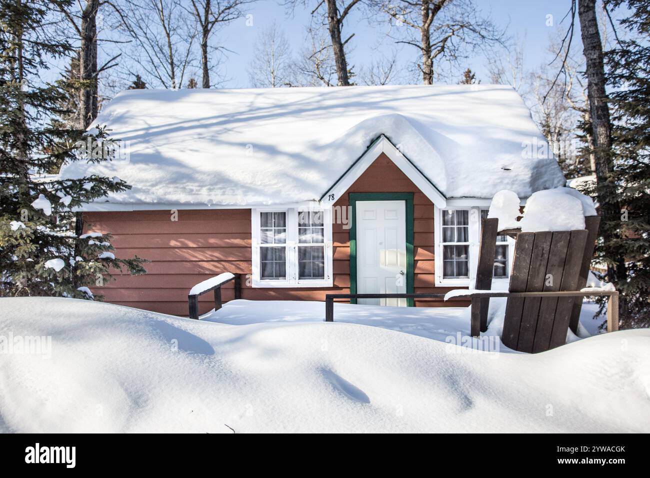 A small cabin in the woods is covered in snow. The house is brown and ...