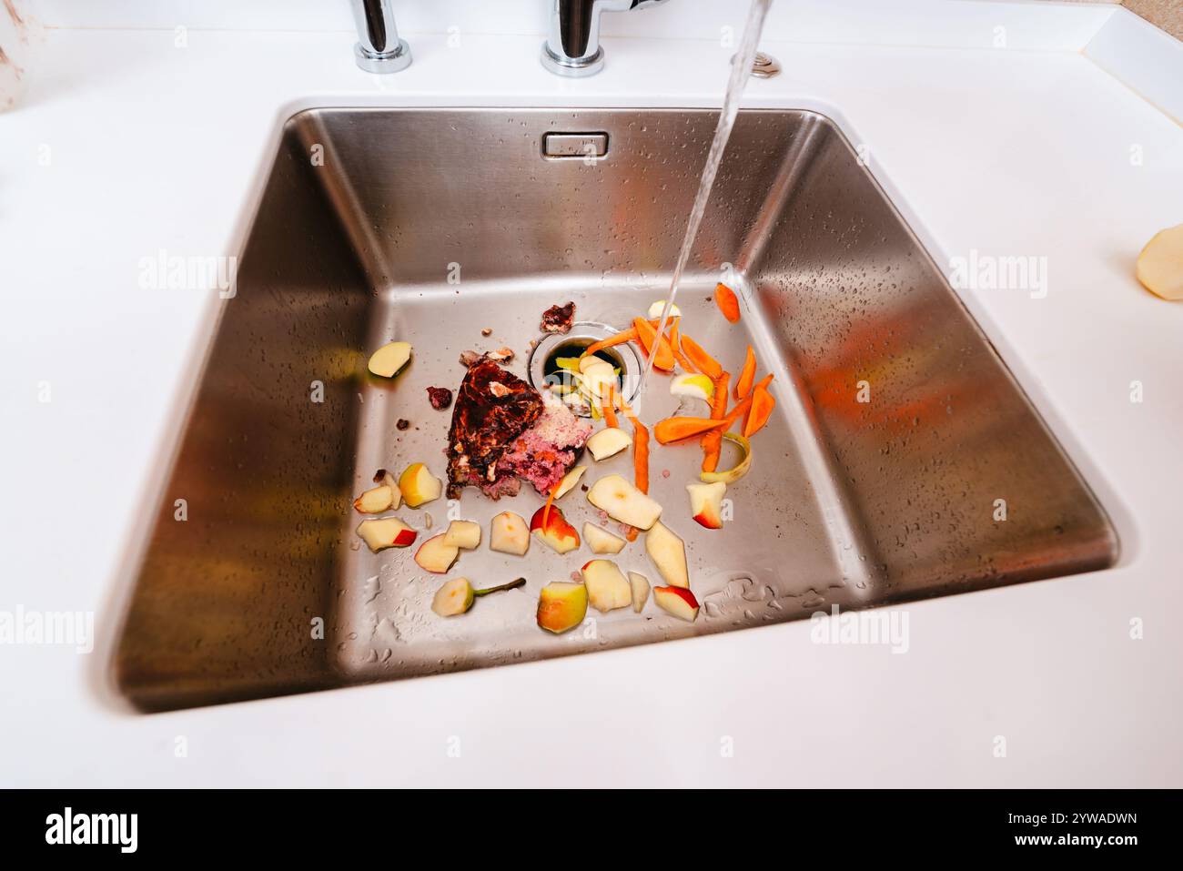 Food waste and vegetable scraps in a kitchen sink with running water ...