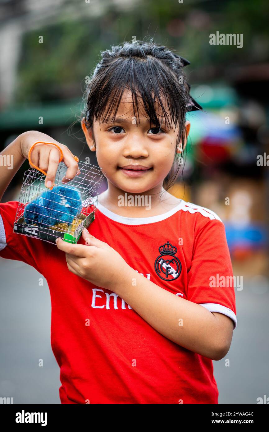 A young Filipino girl holds a chic dyed blue in a tiny cage in Manila ...