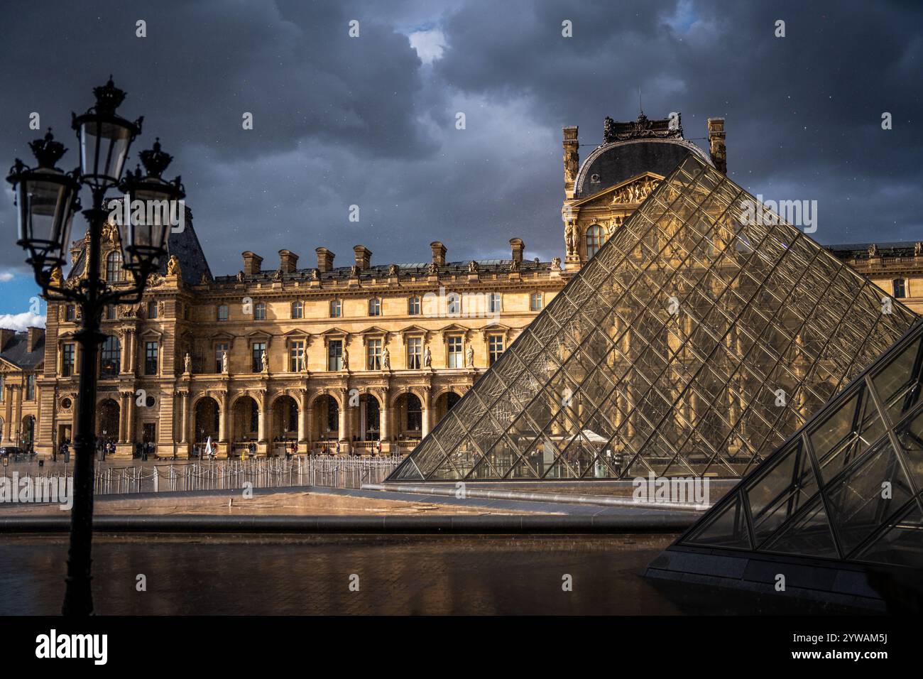 Louvre pyramid under the sun with the ground wet after a day of rain ...