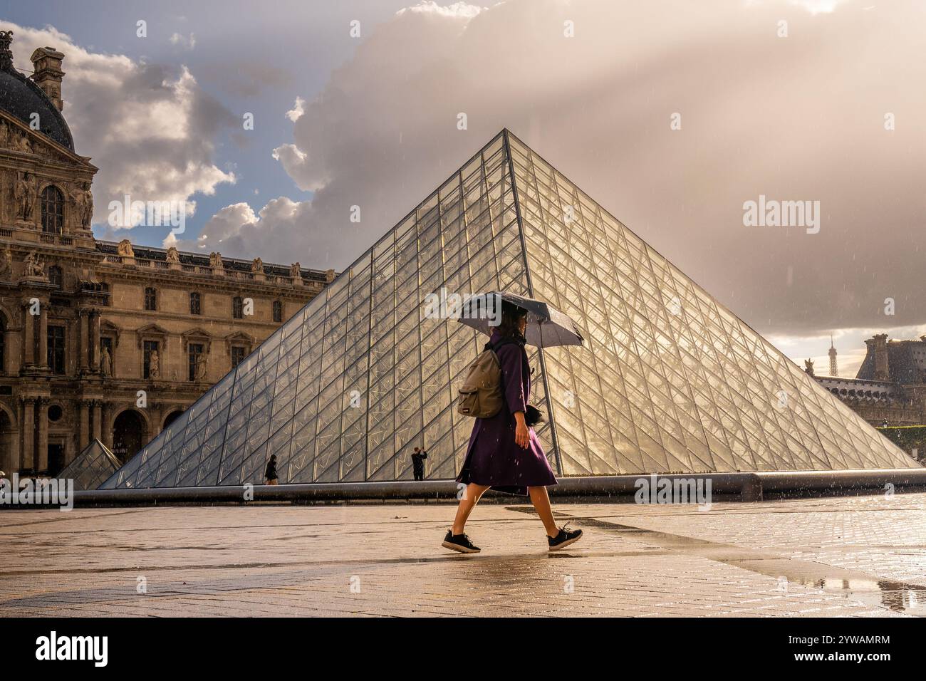 girl walking with an umbrella in front of the pyramid of the louvre ...