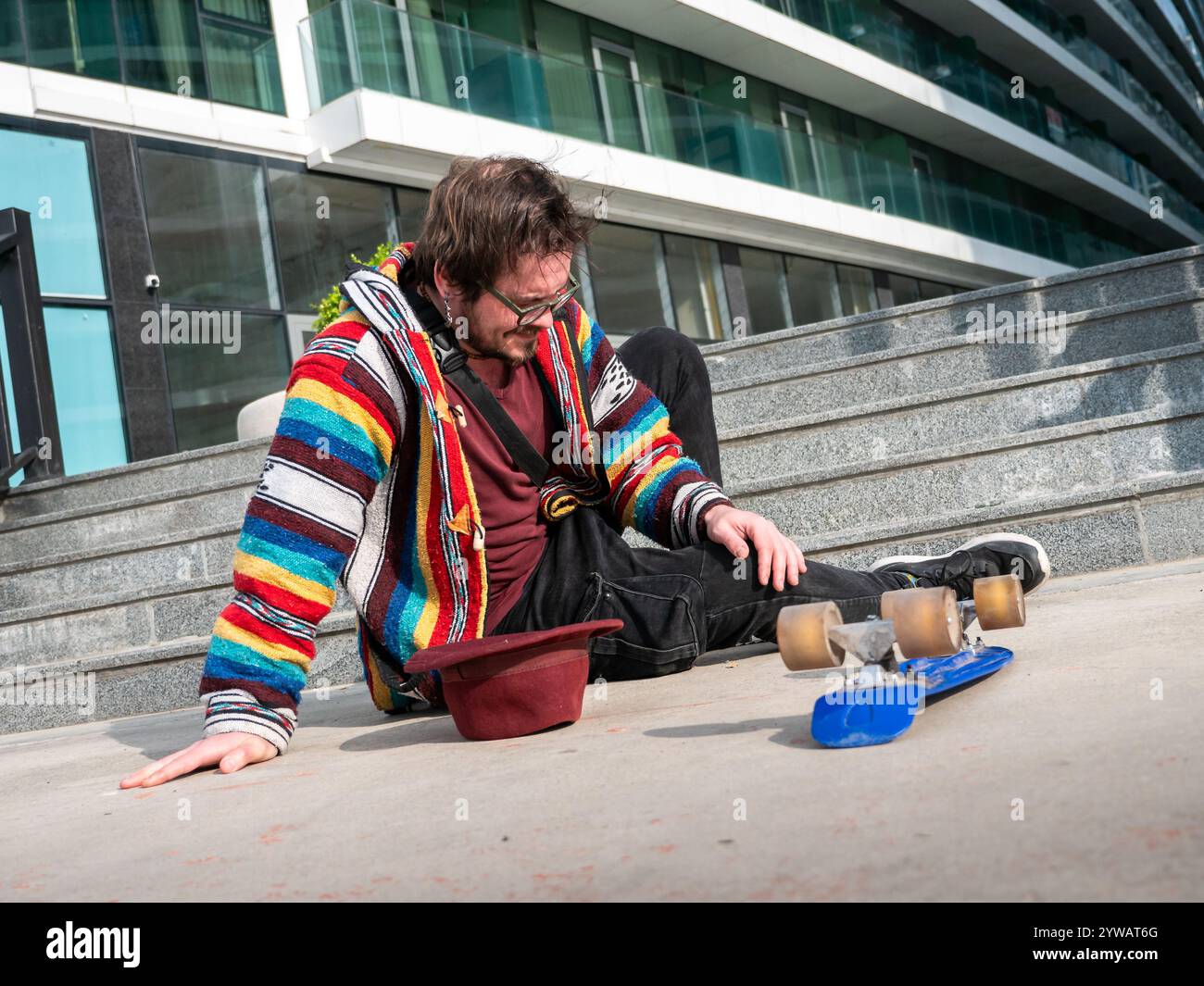 Skateboarder sitting on pavement after fall, wearing colorful striped ...