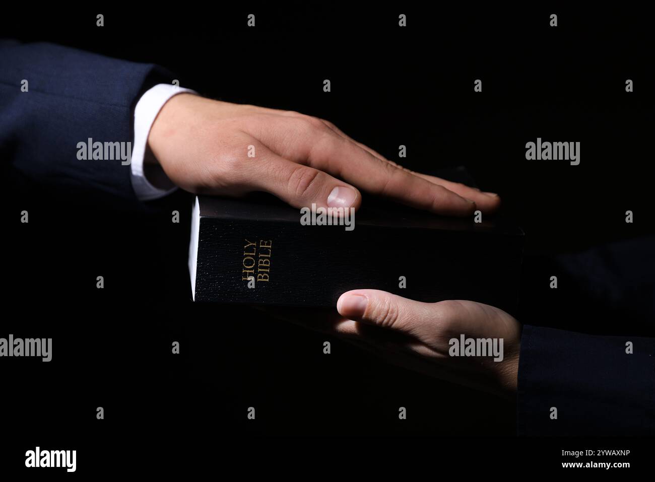 Man taking oath with his hand on Bible against black background ...