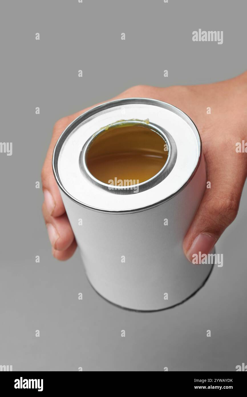 hand holding yellow adhesive in silver tin can isolated gray background ...