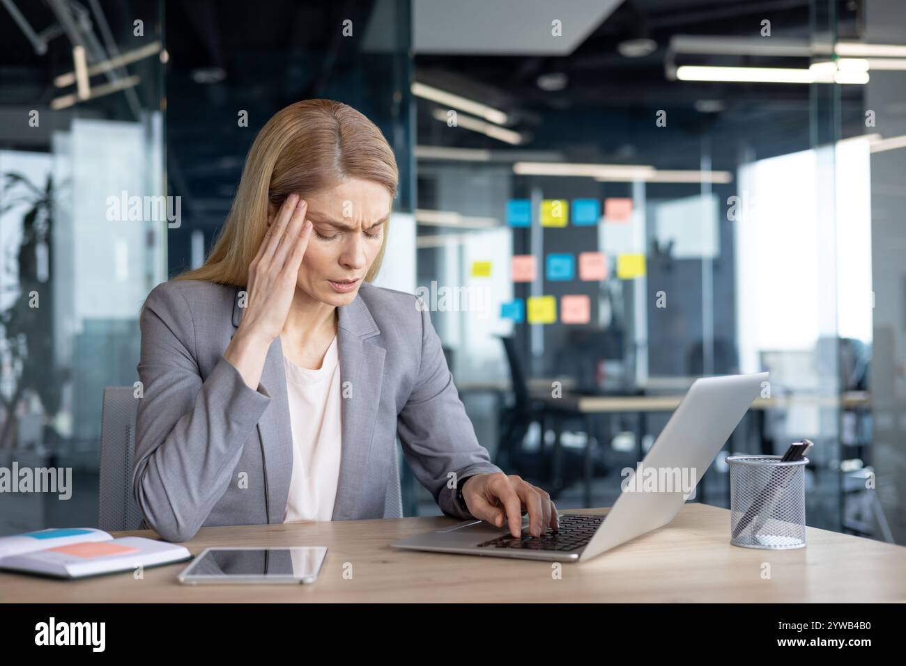 A businesswoman experiencing stress and headache works on her laptop in ...