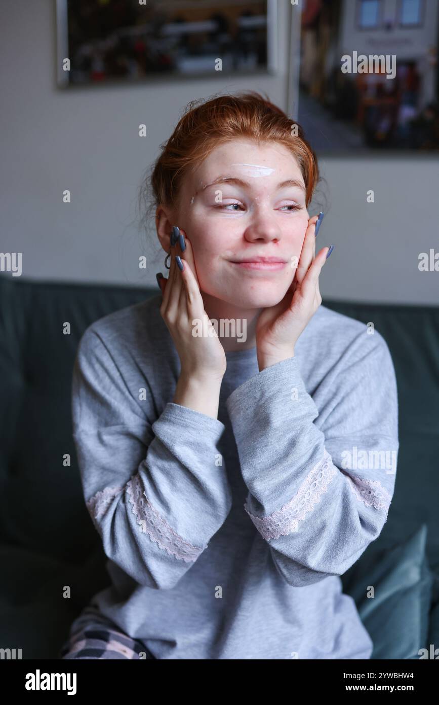 Girl caring of her beautiful skin on the face. Applying moisturizer on ...