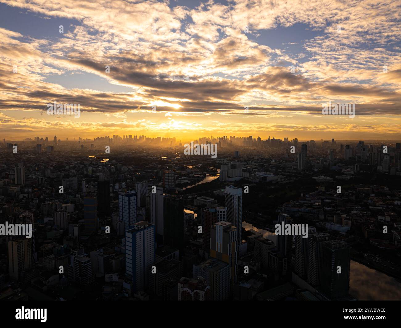Manila city skyline with skyscrapers and buildings glowing in the golden sunset with clouds and ...