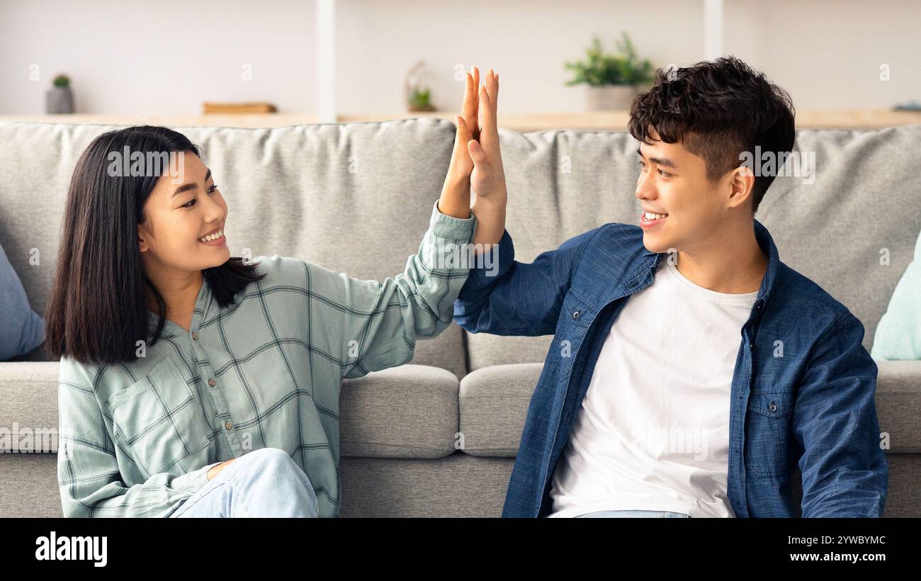 Tired asian couple sitting on floor, giving high five Stock Photo - Alamy