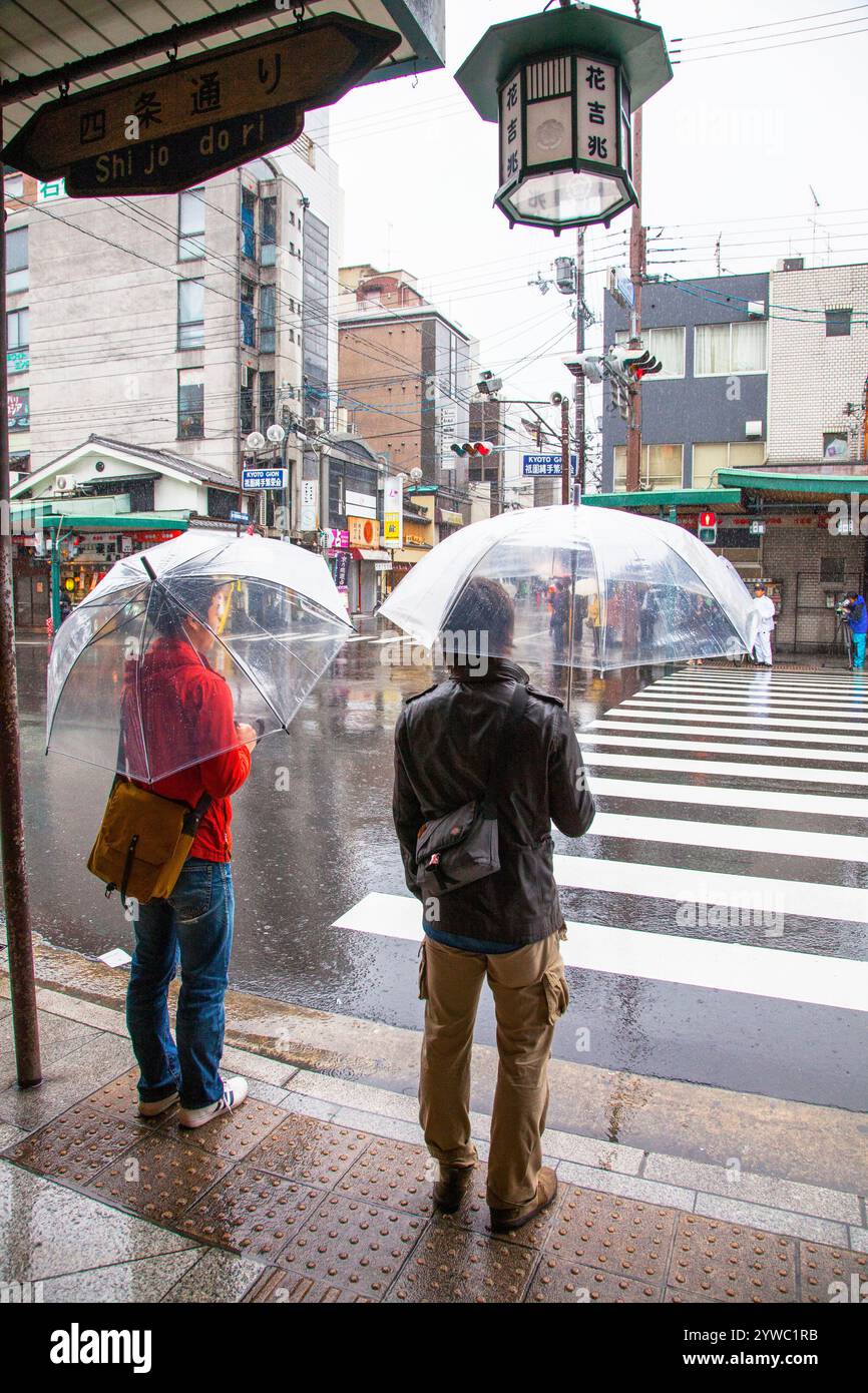 Two Japanese people with umbrellas waiting to cross Shijo-dori street ...