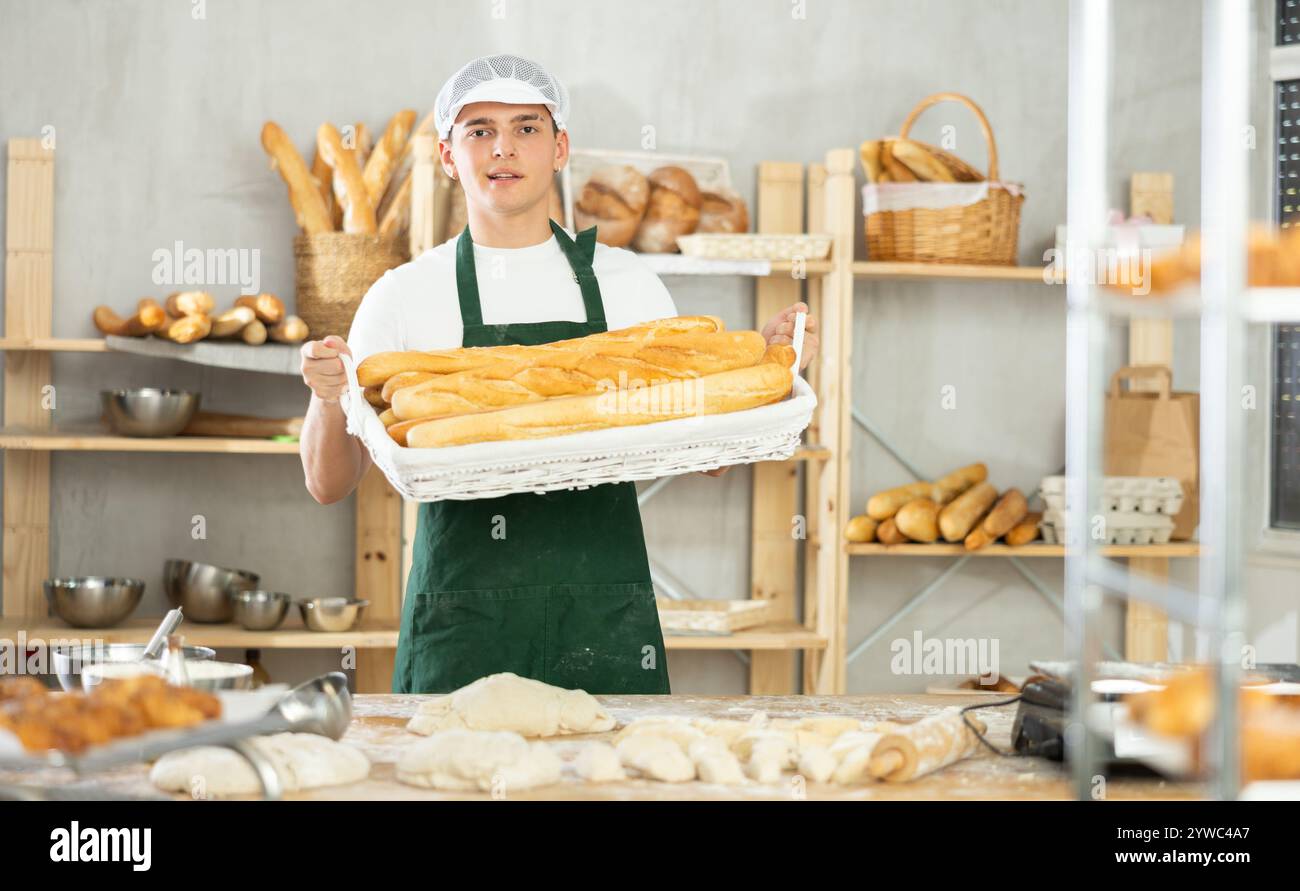 Happy male baker posing with basket of freshly baked baguettes in ...