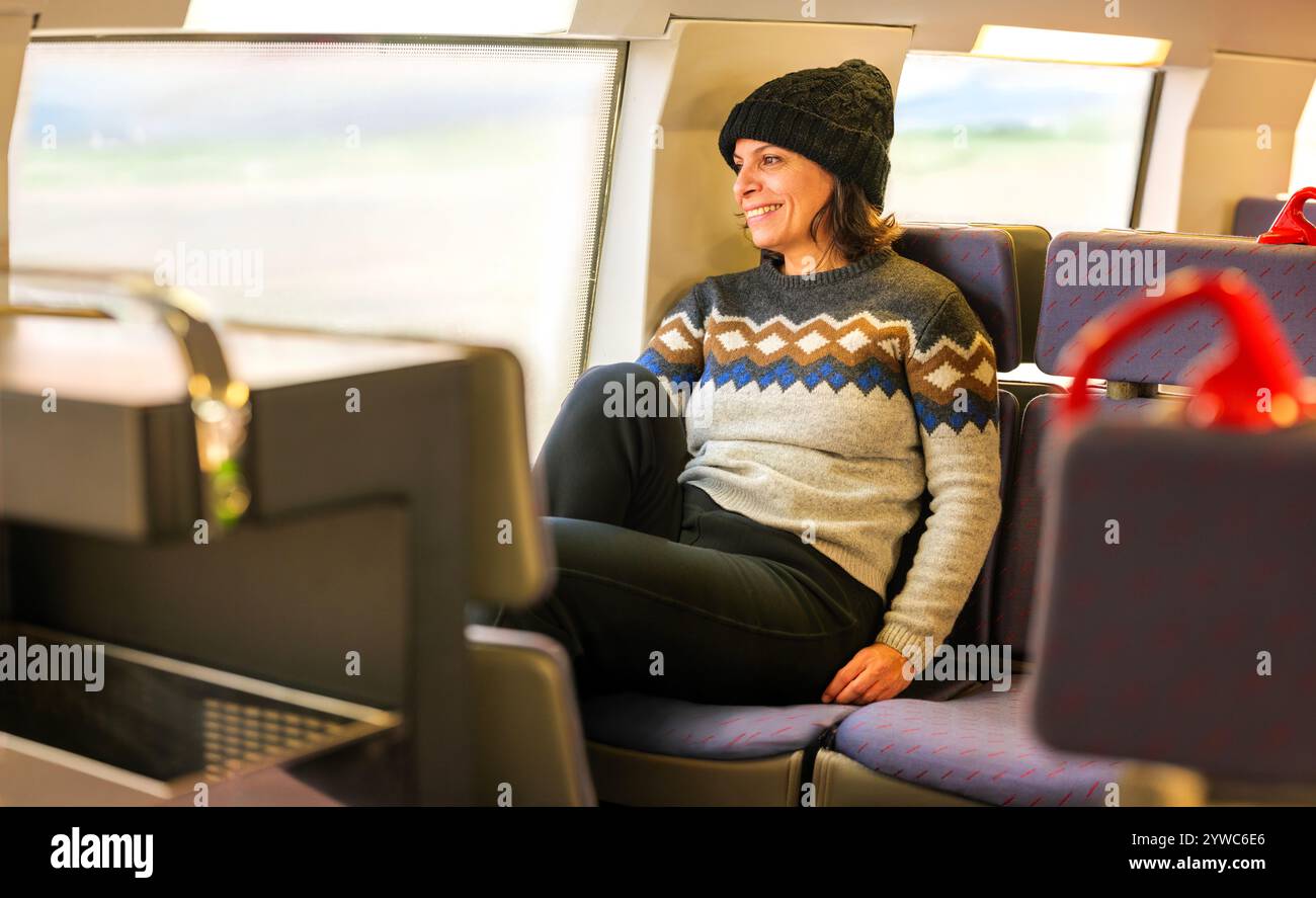 A smiling passenger gazing out of her train carriage window, savoring ...