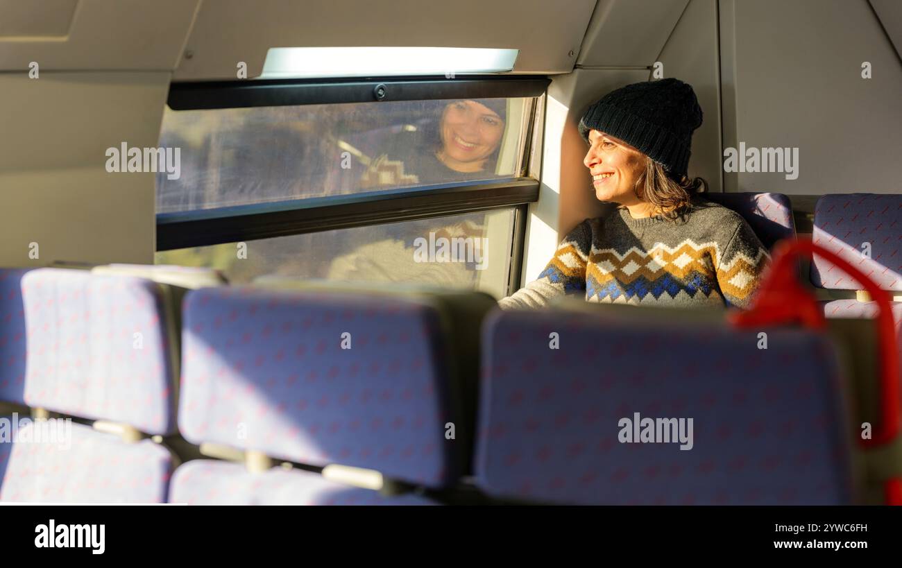 A smiling passenger gazing out of her train carriage window, savoring ...