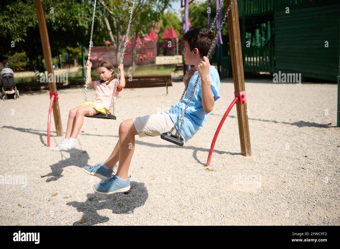 Two children play joyfully on swings in a sunny park, enjoying the ...