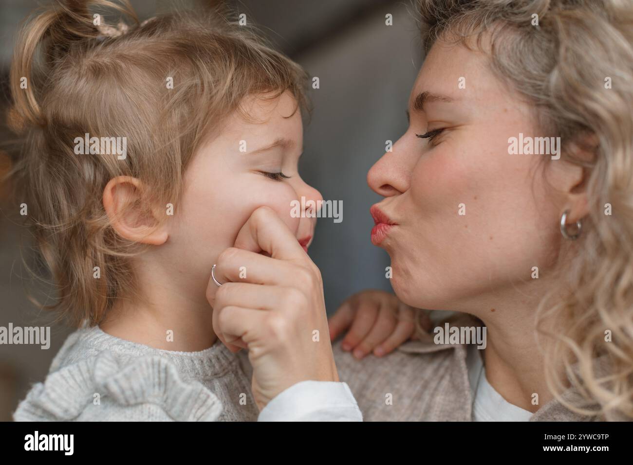 Close-up of a woman pinching her daughter's cheek and puckering her ...