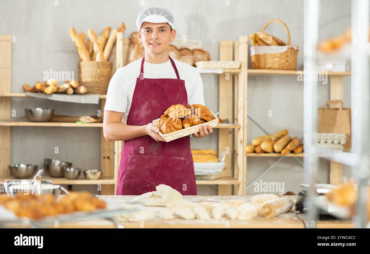 Positive male baker in uniform stands behind counter in small private ...
