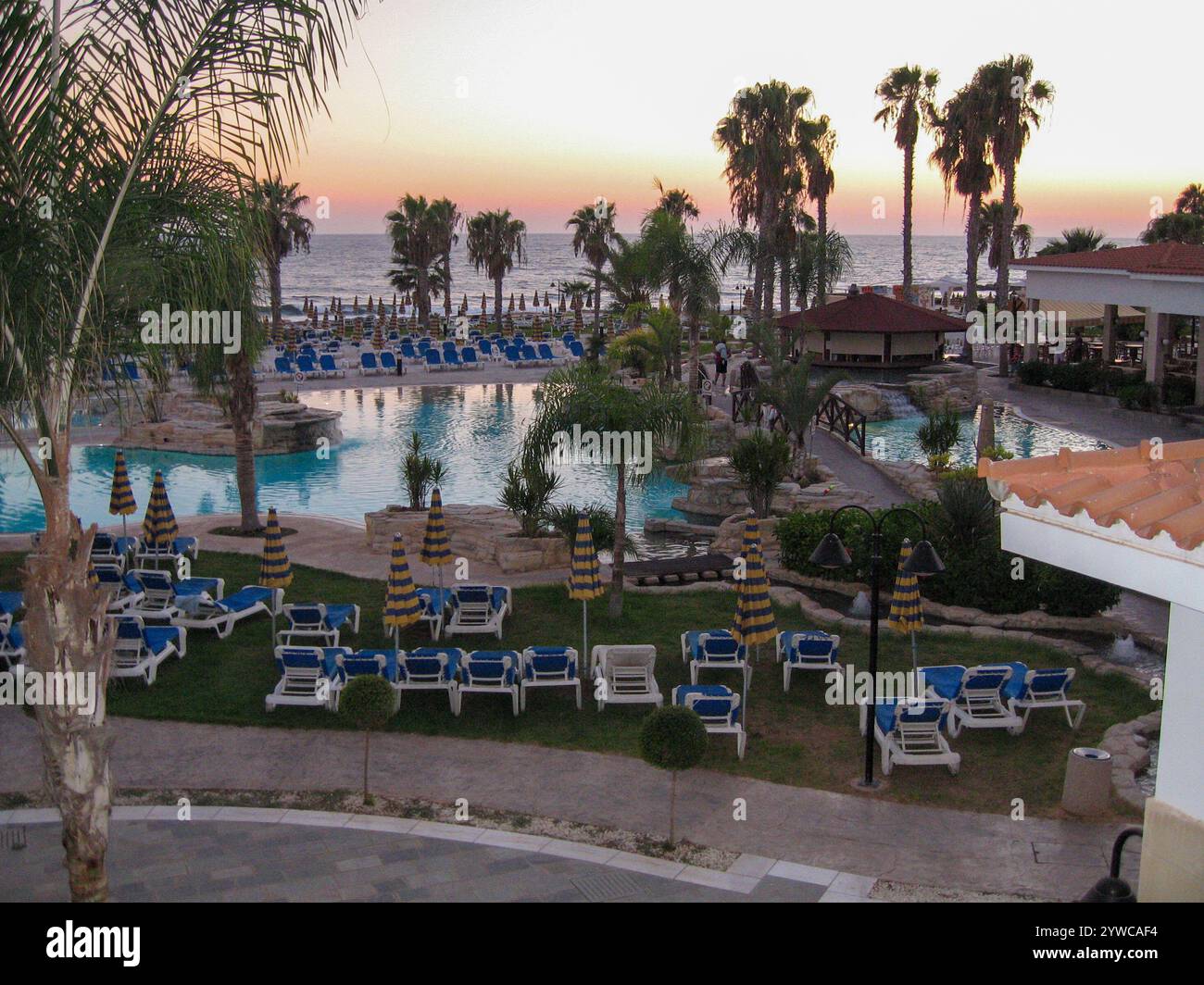 Guests unwind by the poolside as the sun sets over the ocean, creating ...