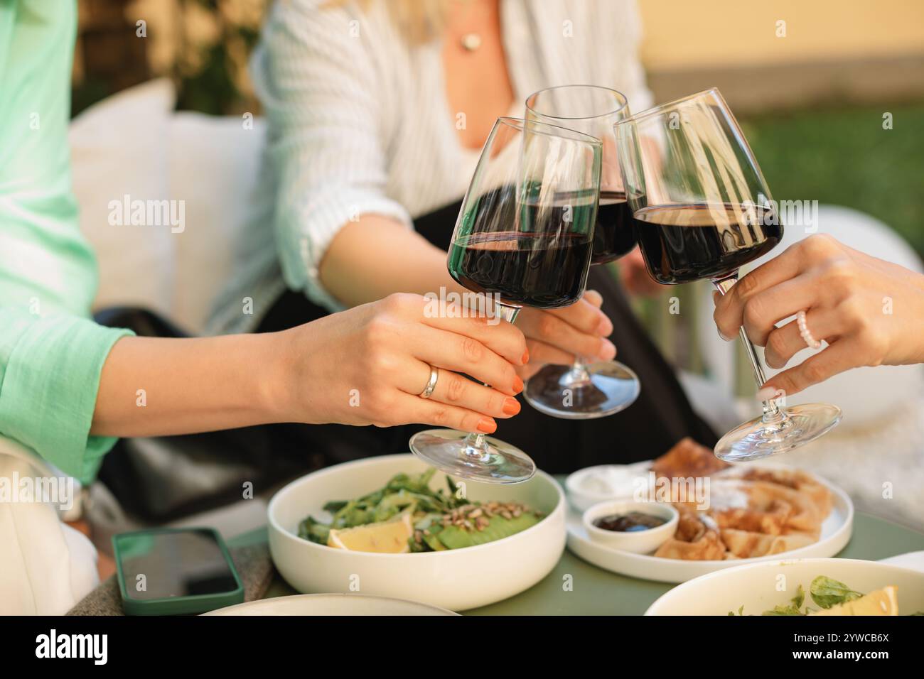 Close-up of three women having lunch outdoors making a celebratory ...