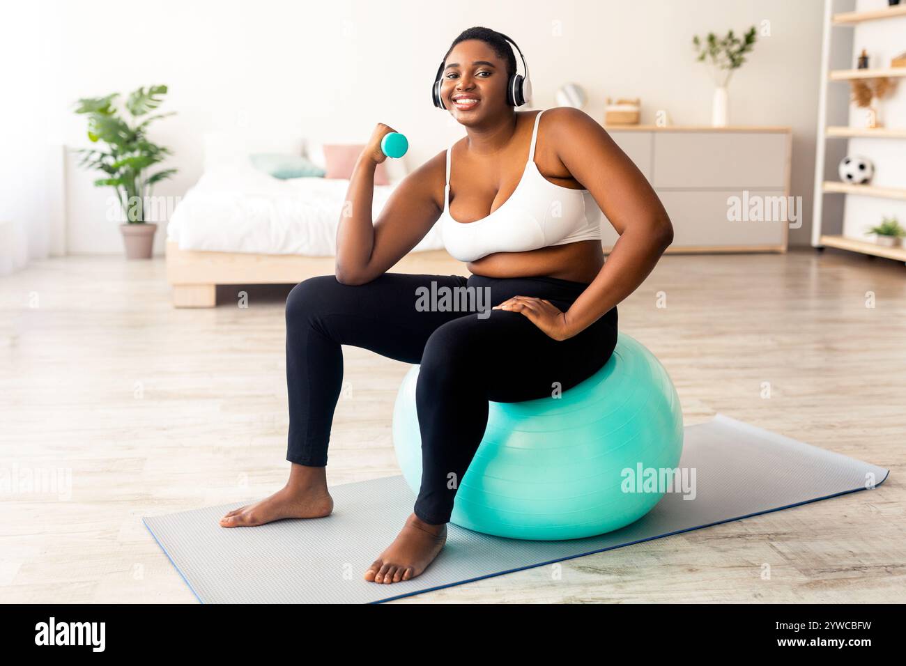 Plus size black woman sitting on fitball, exercising with dumbbells ...