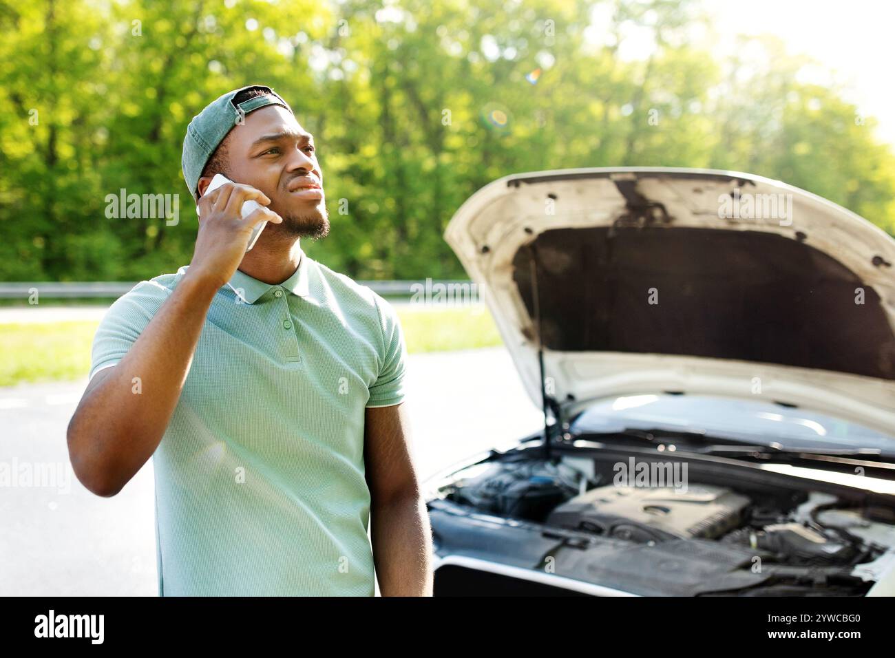 Stressed black guy standing near broken vehice, having mobile phone ...
