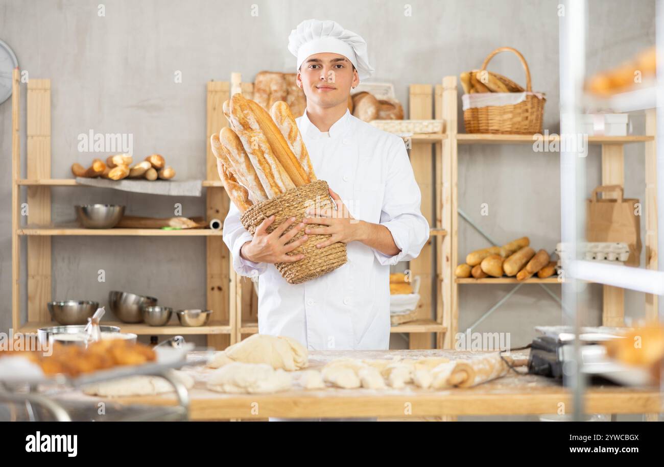 Happy male baker posing with basket of freshly baked baguettes in ...