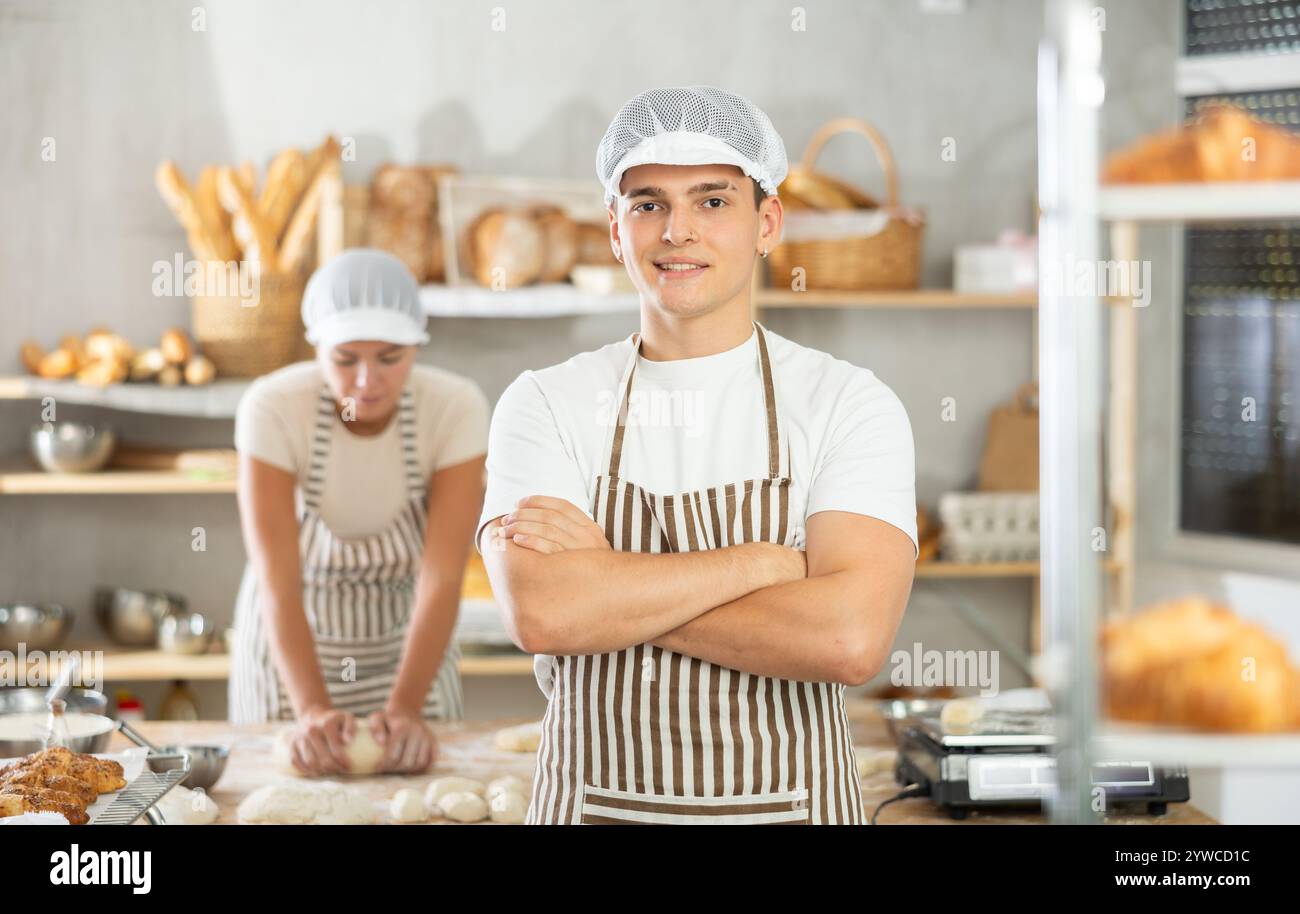 Dedicated young baker standing with arms crossed in bakery Stock Photo ...