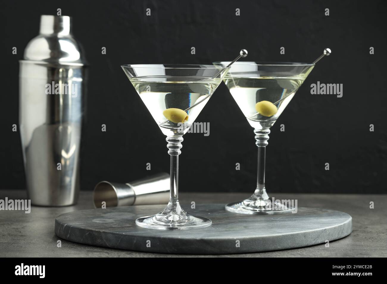 Martini cocktail with olives in glasses on grey table against black ...