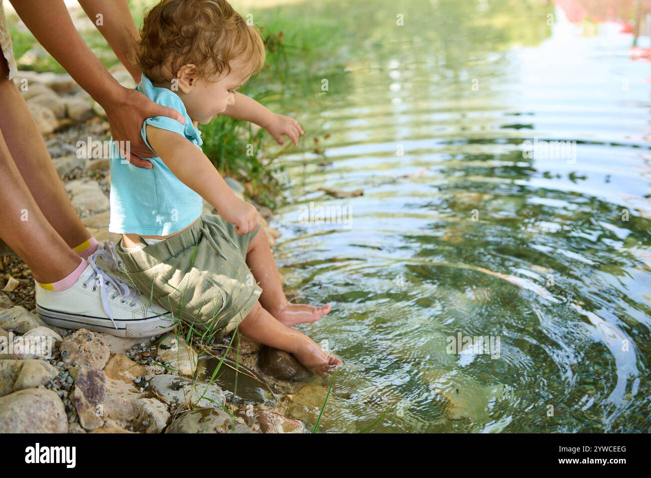 A parent helps their toddler explore nature by dipping his feet into a ...